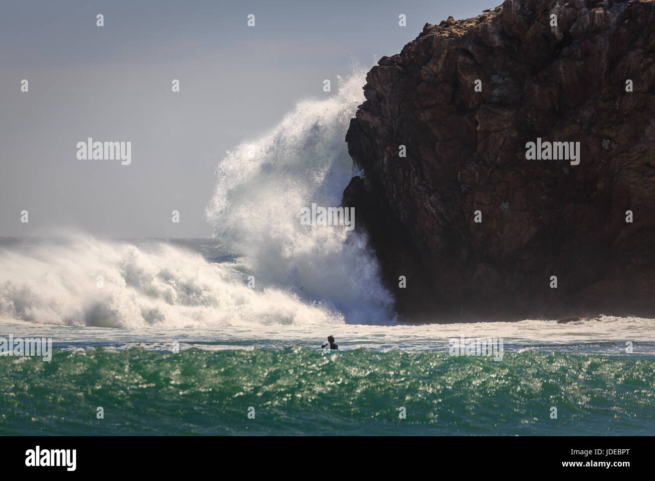 Big wave crashing crashing on rocks as a surfer waits for a wave Stock ...