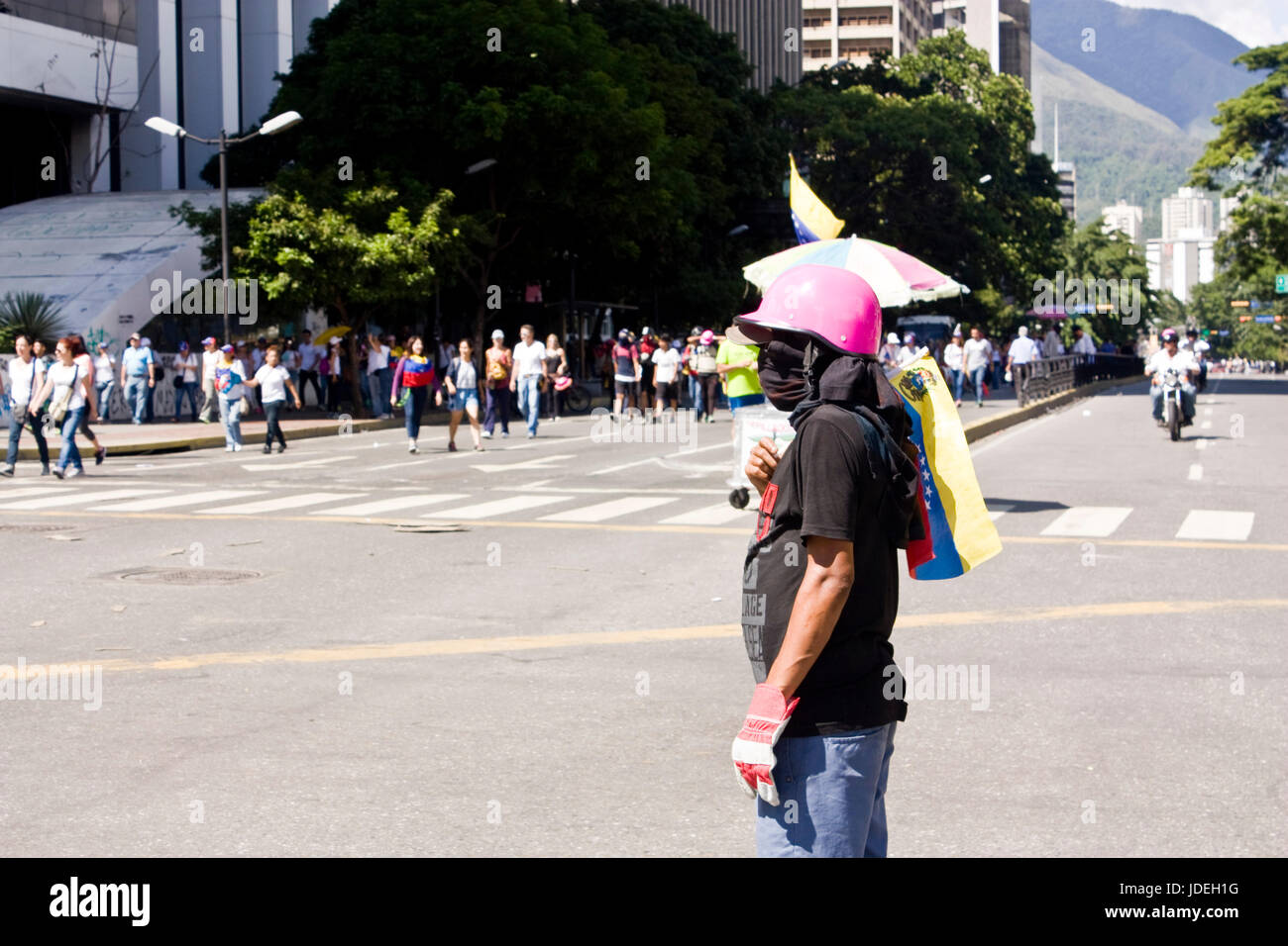 A hooded demonstrator holding the flag of Venezuela stands on a street ...