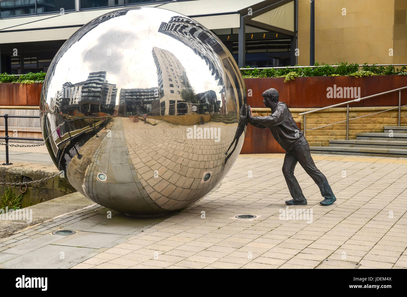 Monument as a Man pushing a huge silver ball in Leeds Dock Stock Photo ...