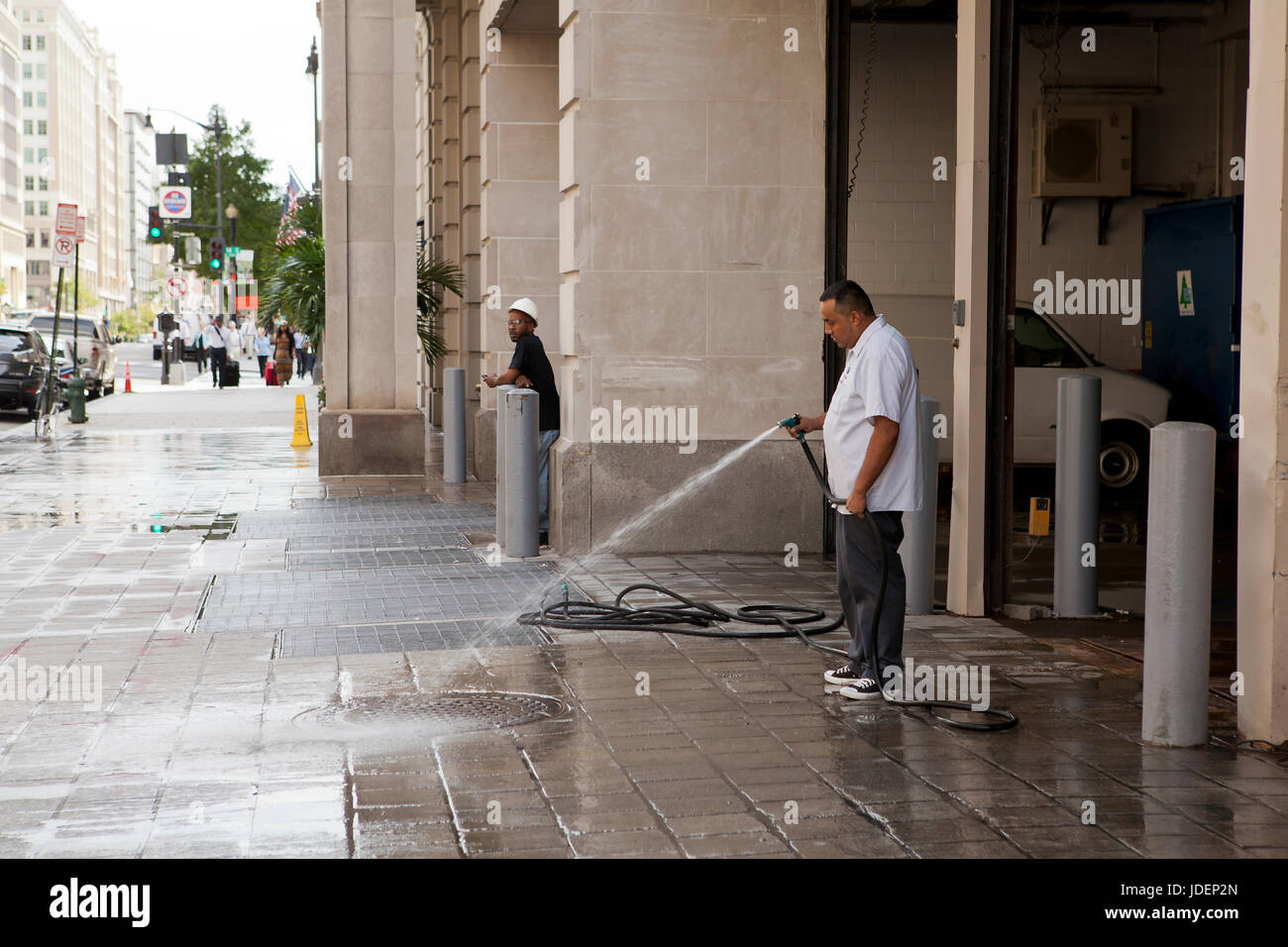 Building maintenance man washing sidewalk / walkway / loading dock ...
