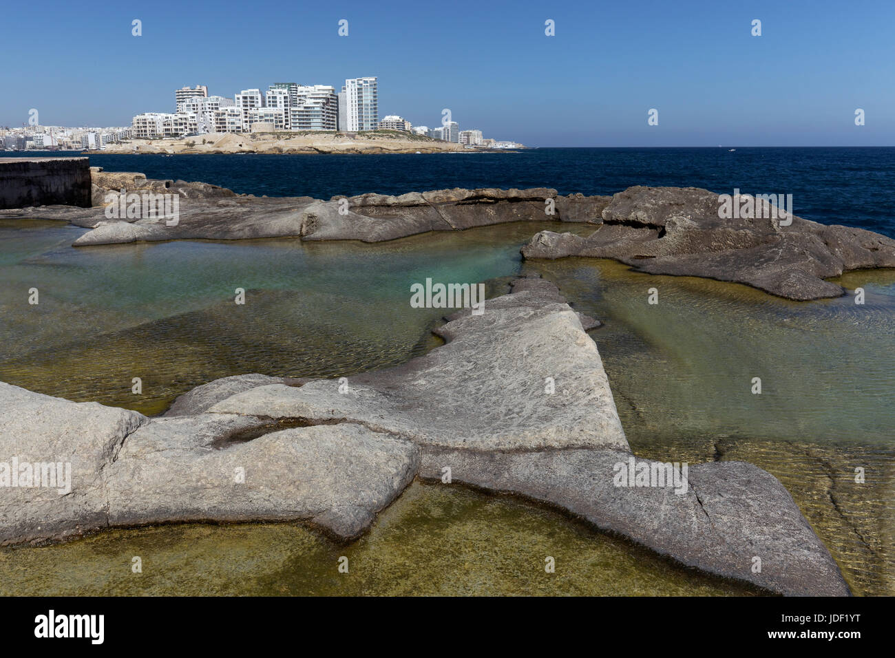 Bizarre rocky coast with natural water basins, view of Sliema, Valletta ...