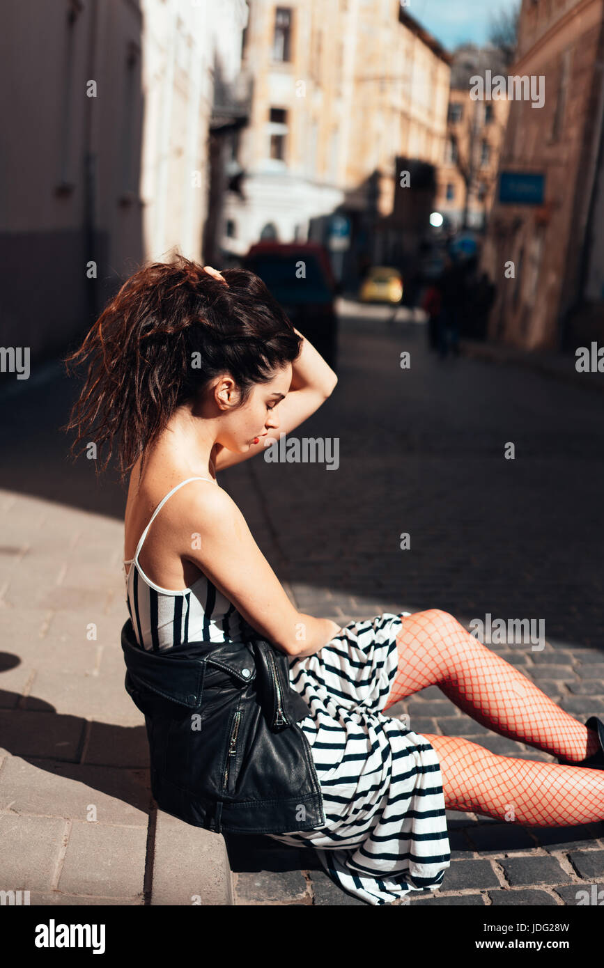 Beautiful fashionable lady sitting on old street Stock Photo - Alamy