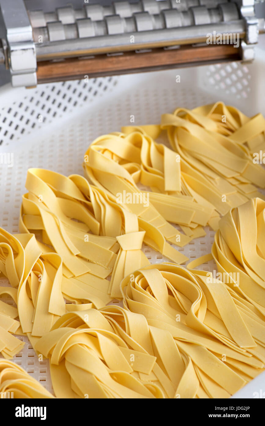 Freshly made ribbons of Italian tagliatelle pasta lying in piles in a ...