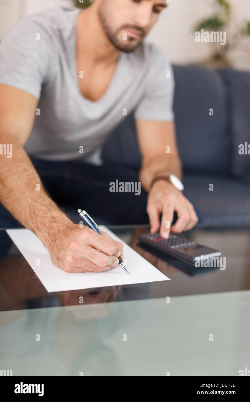 Young caucasian man doing calculation at home with calculator on blank ...