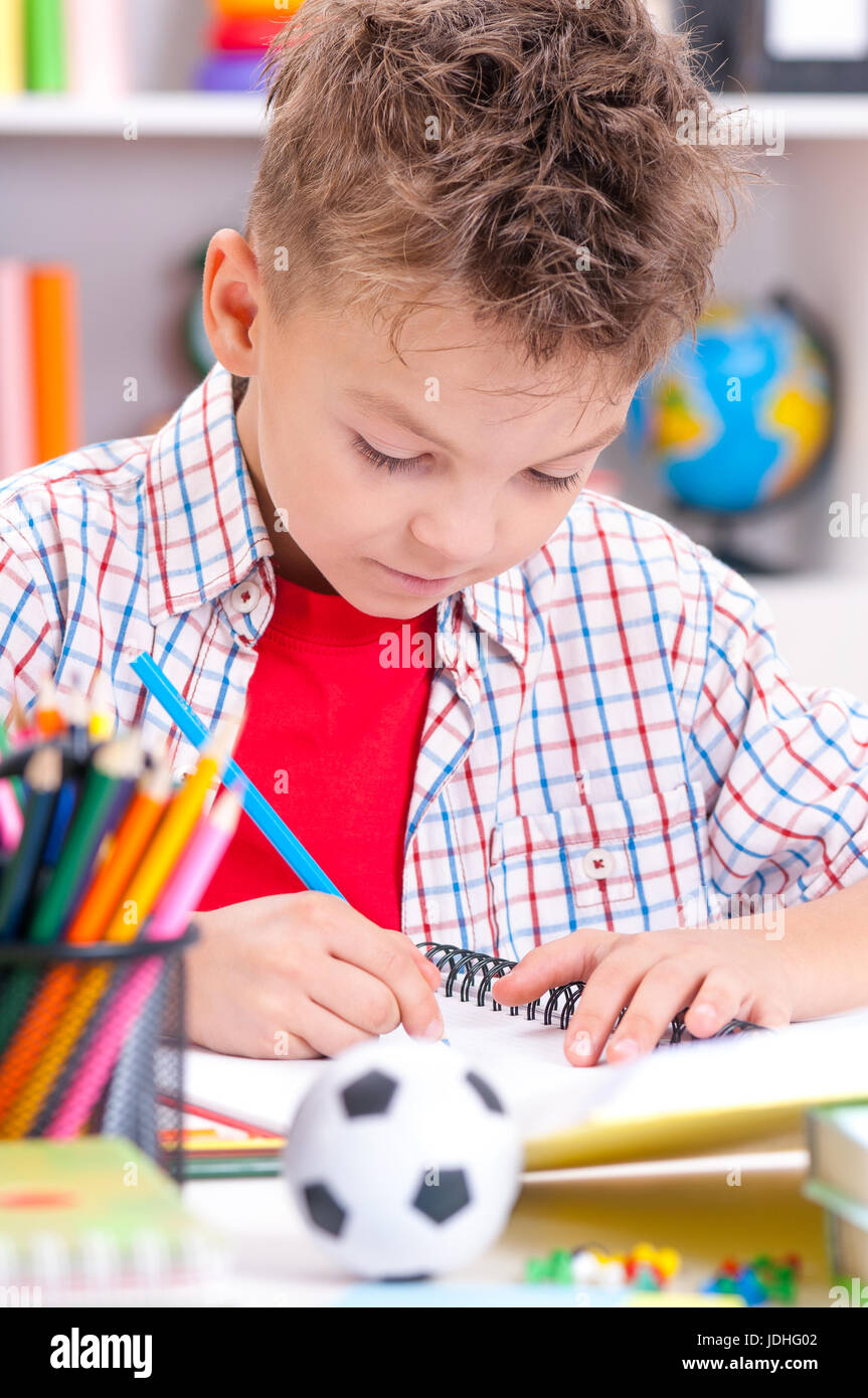 Young boy sitting at desk in the classroom, doing homework at the table ...