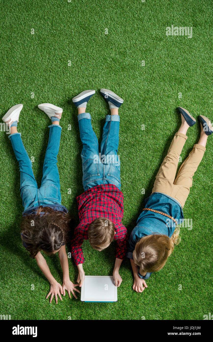 overhead view of children using digital tablet while lying on grass ...