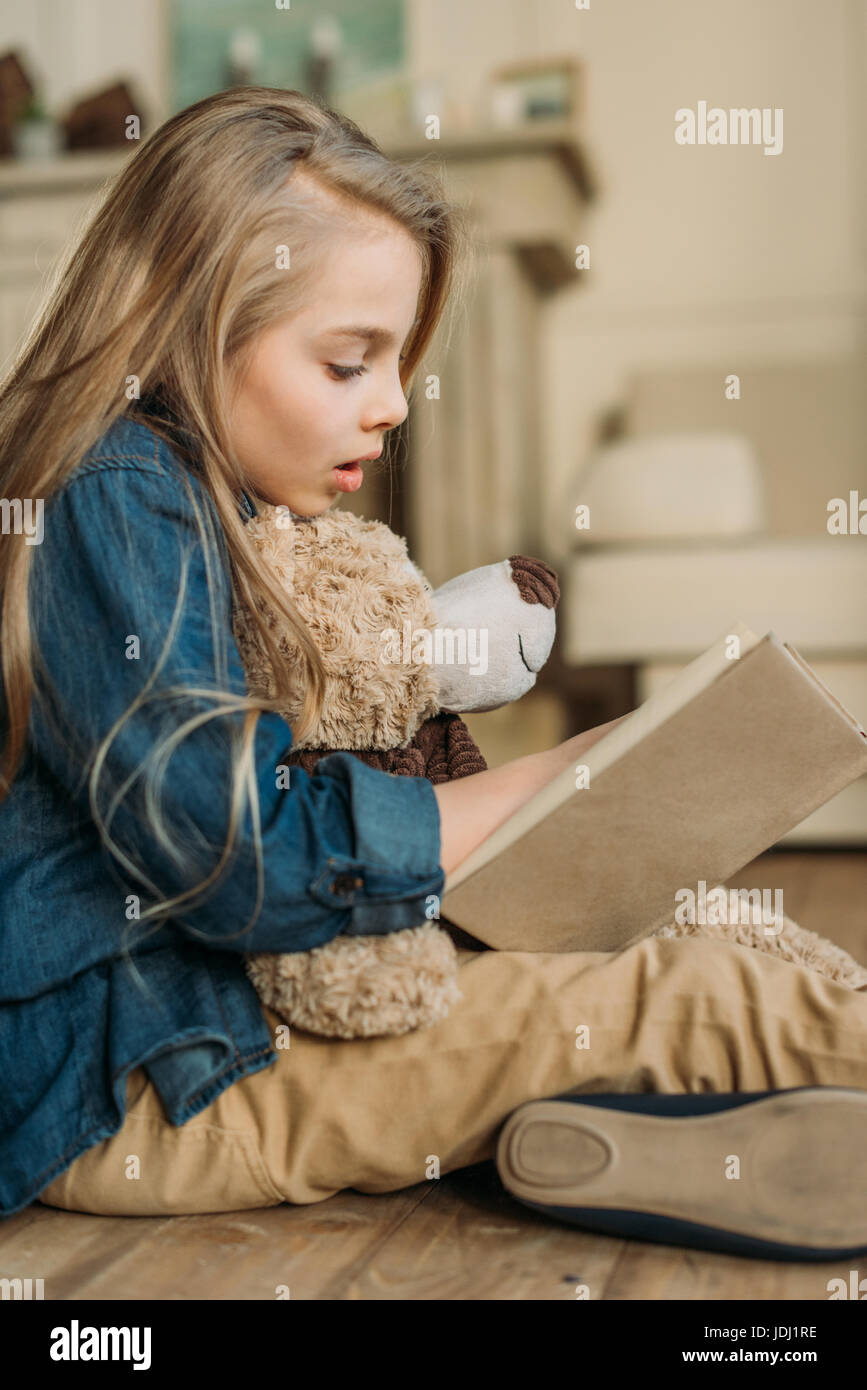 side view of little girl with teddy bear reading book, education kids ...