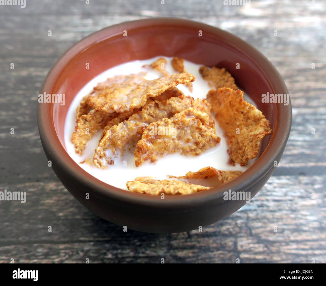 Wheat bran breakfast cereal with milk in clay bowl on wooden background ...