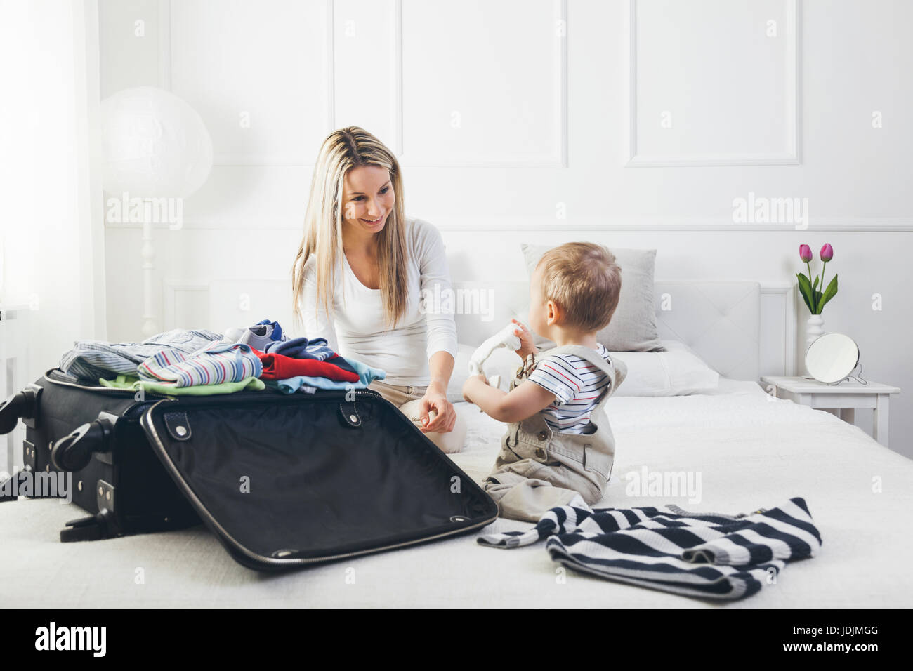 Travelling with kids. Happy mother with her child packing clothes for ...