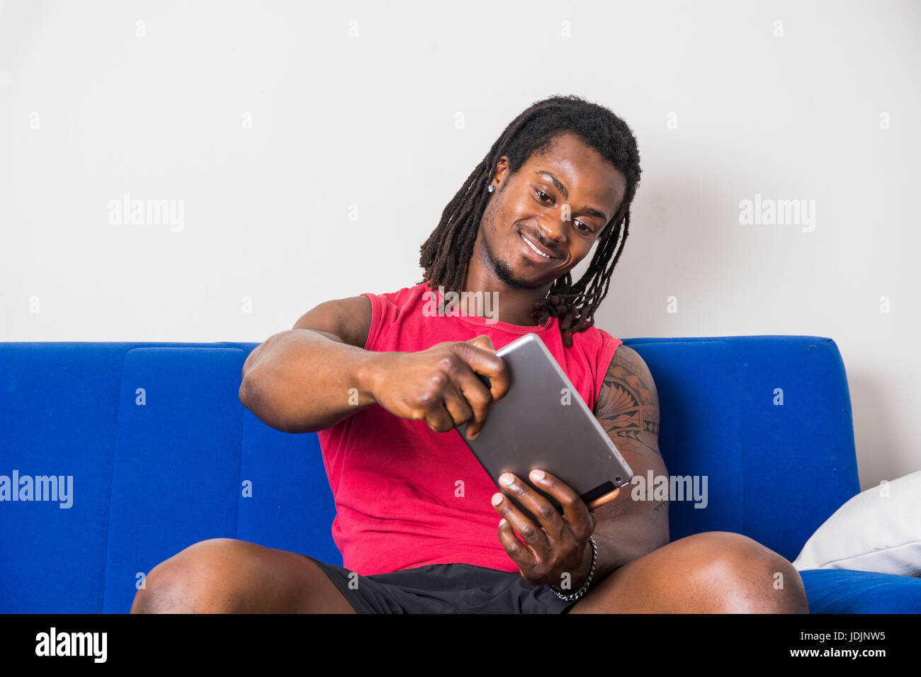 Handsome muscular black man playing videogame on tablet PC, sitting on ...