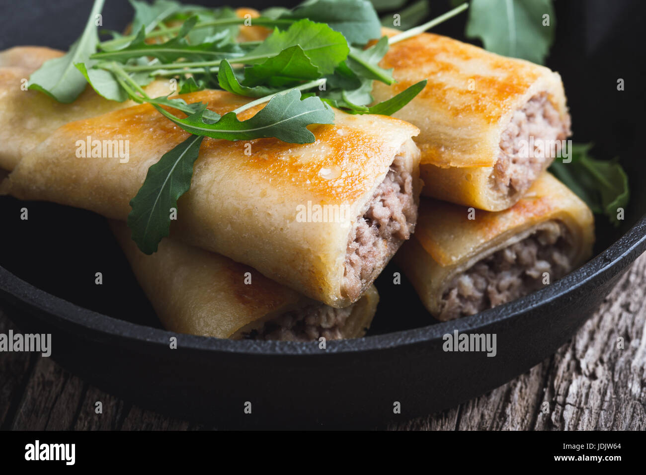 Homemade minced meat rolled crepes served in cast iron pan on rustic ...
