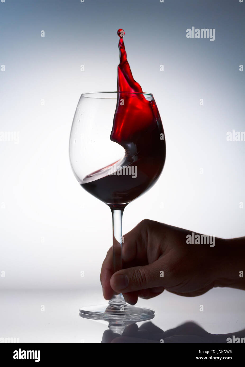 Hand holding glass of red wine with splash Stock Photo - Alamy