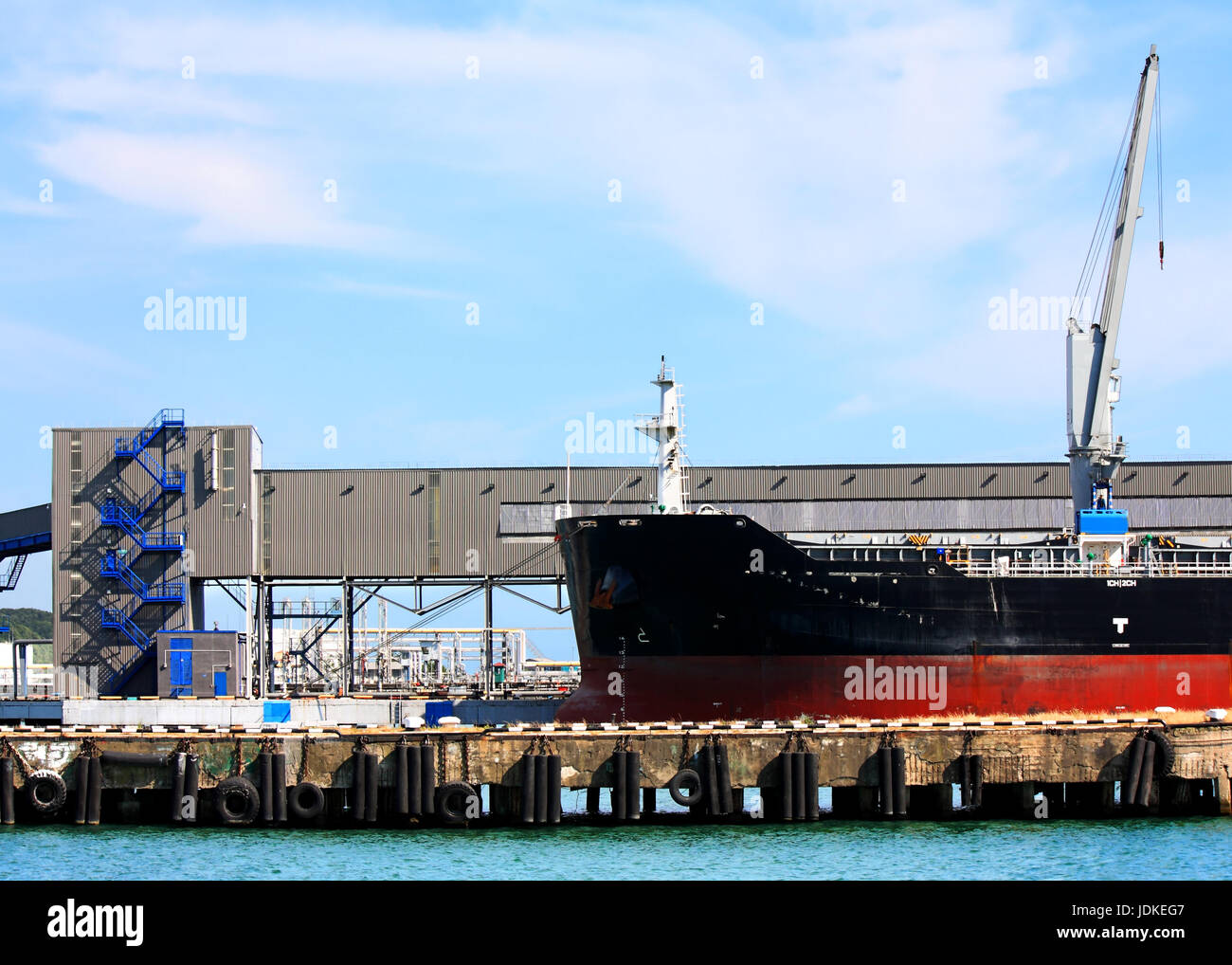 Port berth with material handling equipment and cargo vessel at anchor ...