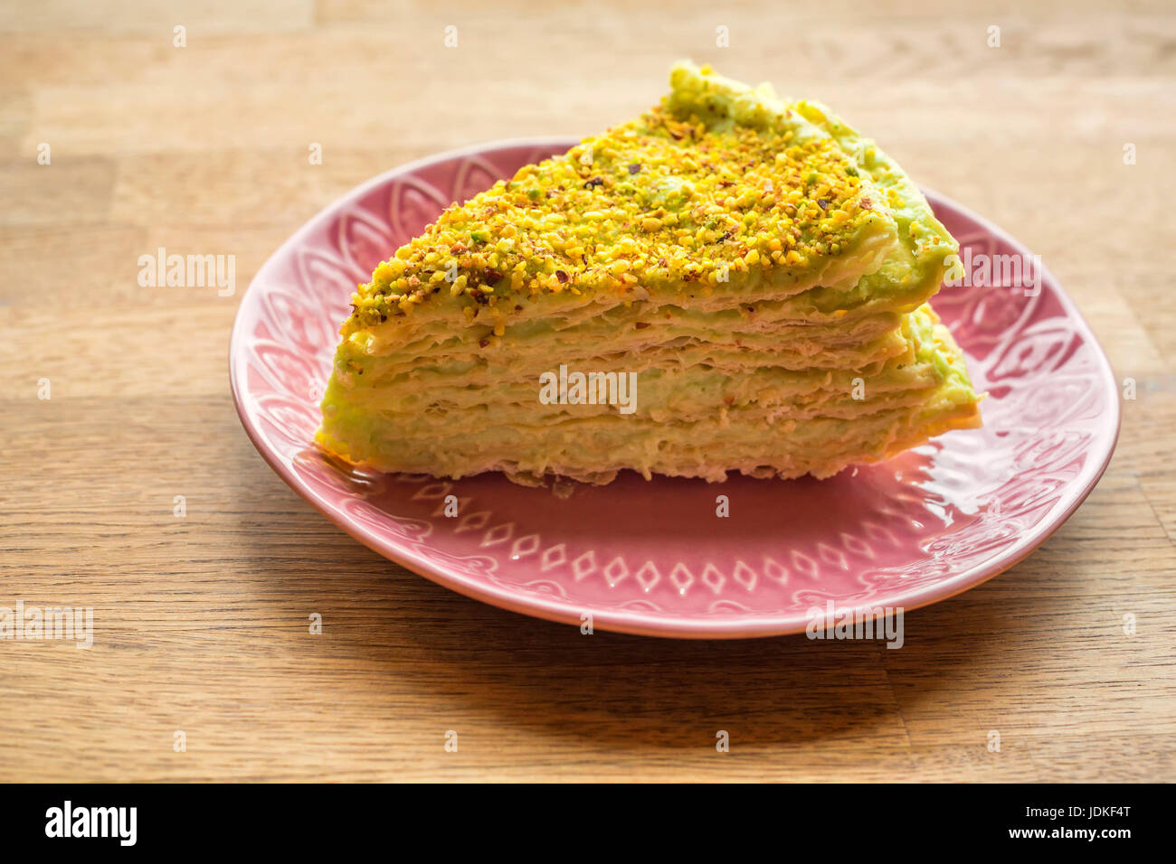French Napoleon cake of puff pistachio pastry with sour cream on a pink ...