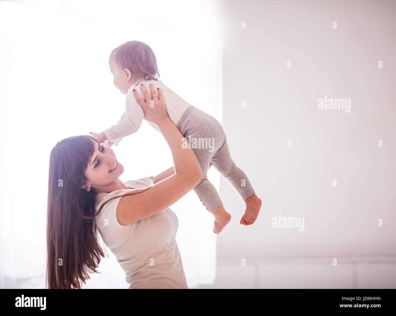 Young mother plays with her little baby girl, opposite the window in ...