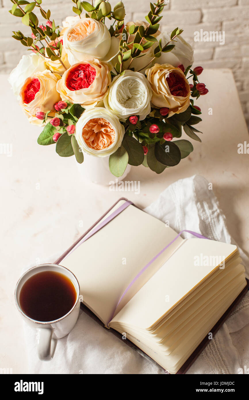 A cup of black tea, notebook and beautiful flowers on the table ...