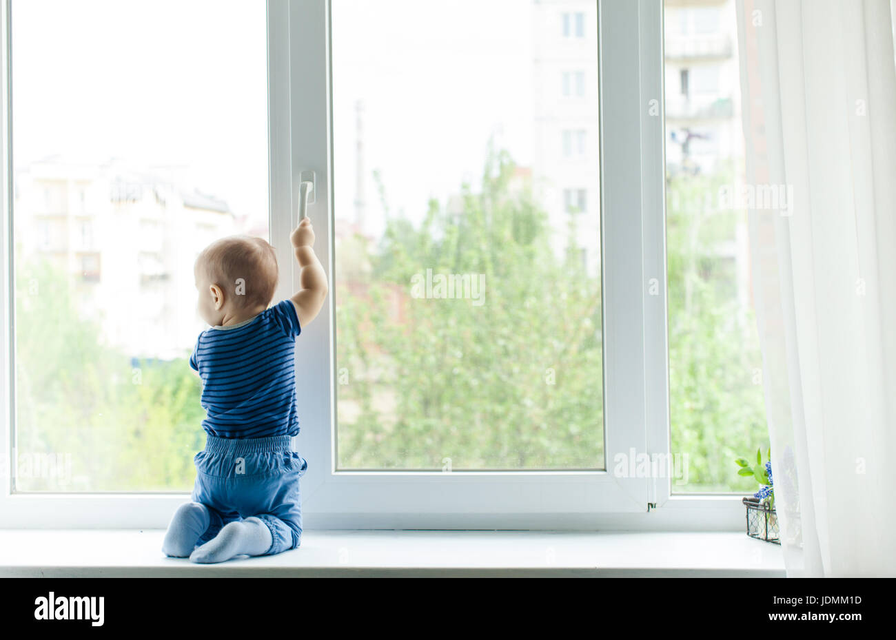 Baby boy sit on the windowsill and trying to open the window pulling ...