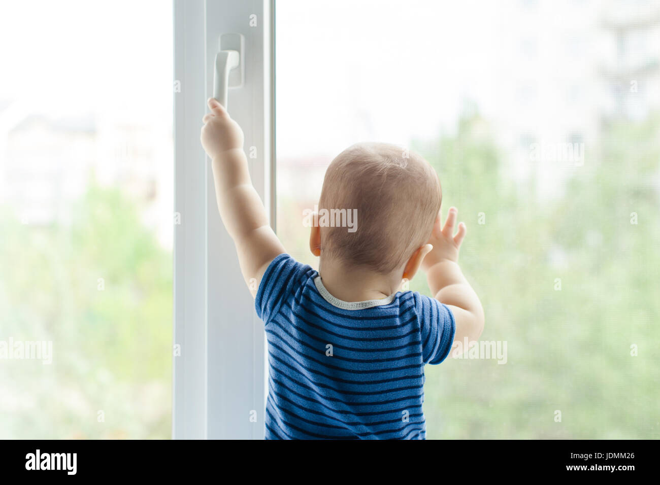 Baby boy sit on the windowsill and trying to open the window pulling ...