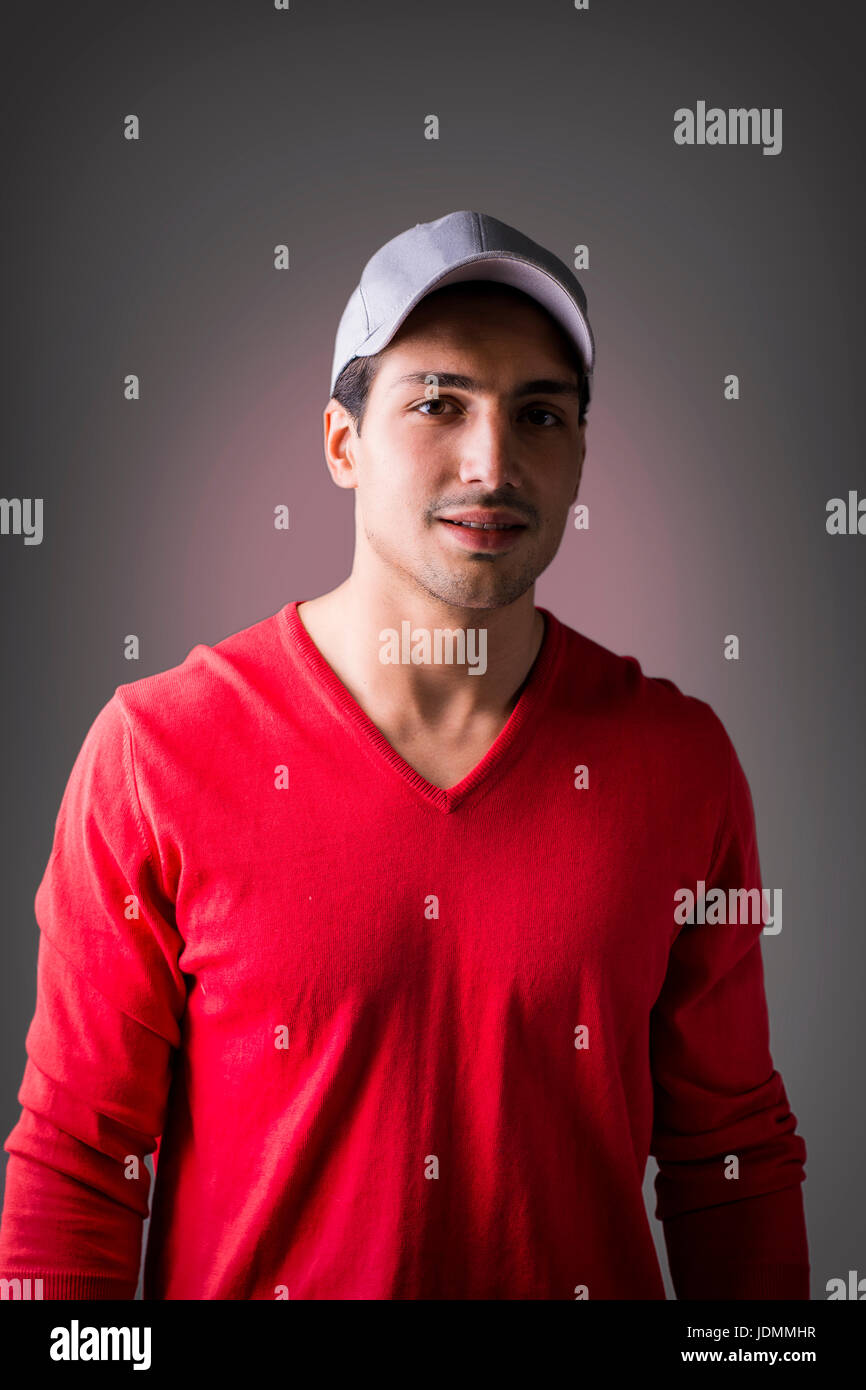 A young man with red wool sweater, wearing baseball cap, front view. On ...