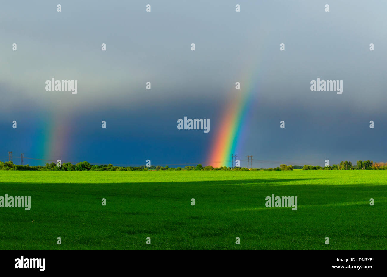 beautiful landscape with green meadow and a bright rainbow far away in ...