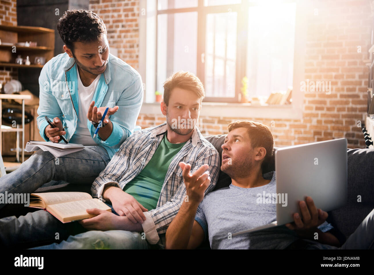 Young professional group sitting together on sofa with laptop and ...