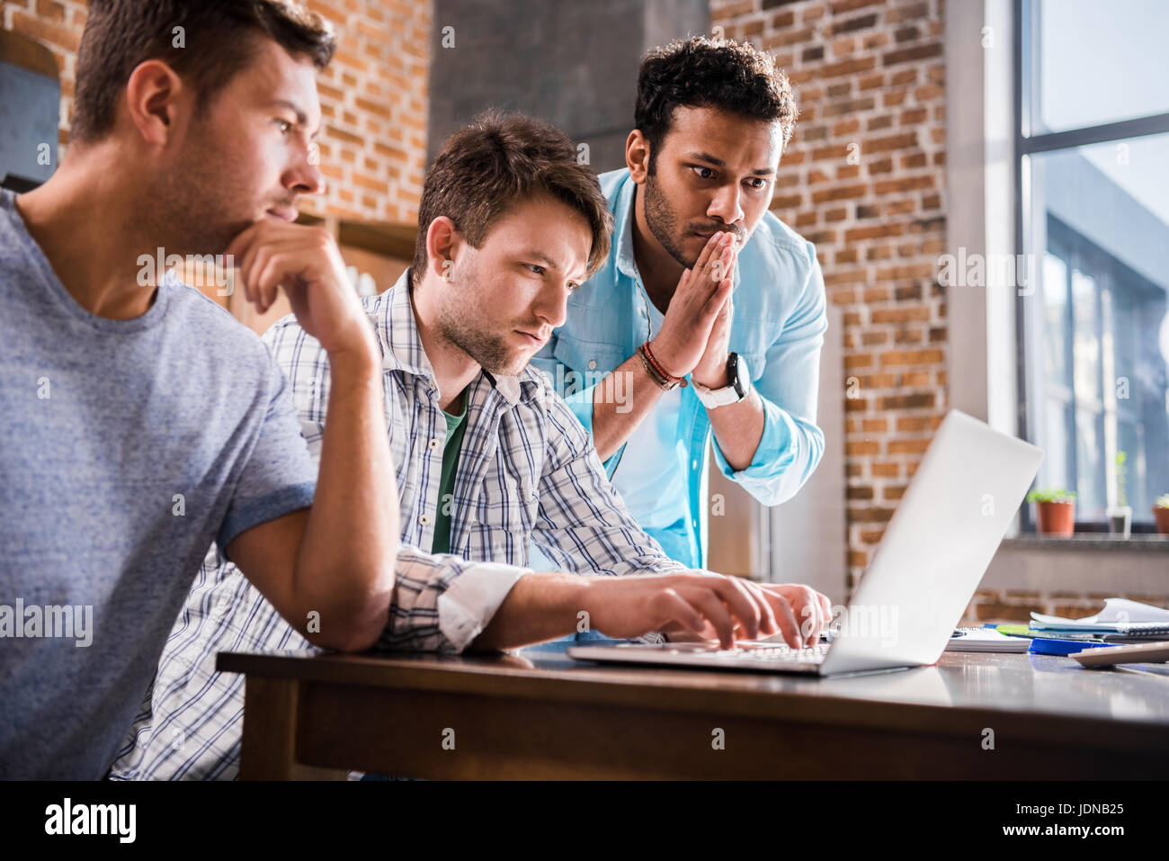 Serious young men using laptop together at home, young professional ...