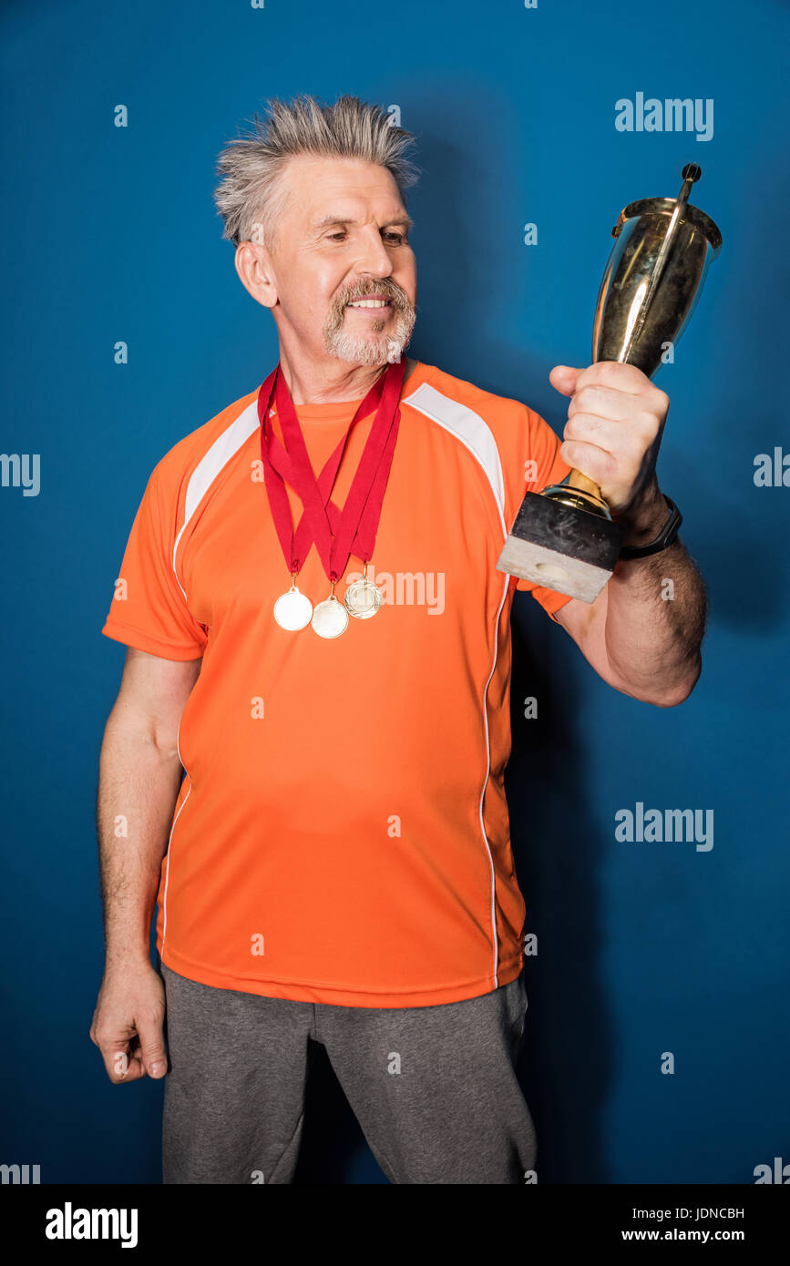 Smiling mature sportsman with medals holding trophy cup isolated on ...
