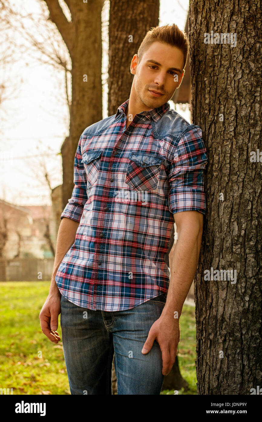 A young man outdoors against a tree, at sunset, with sun behind him ...