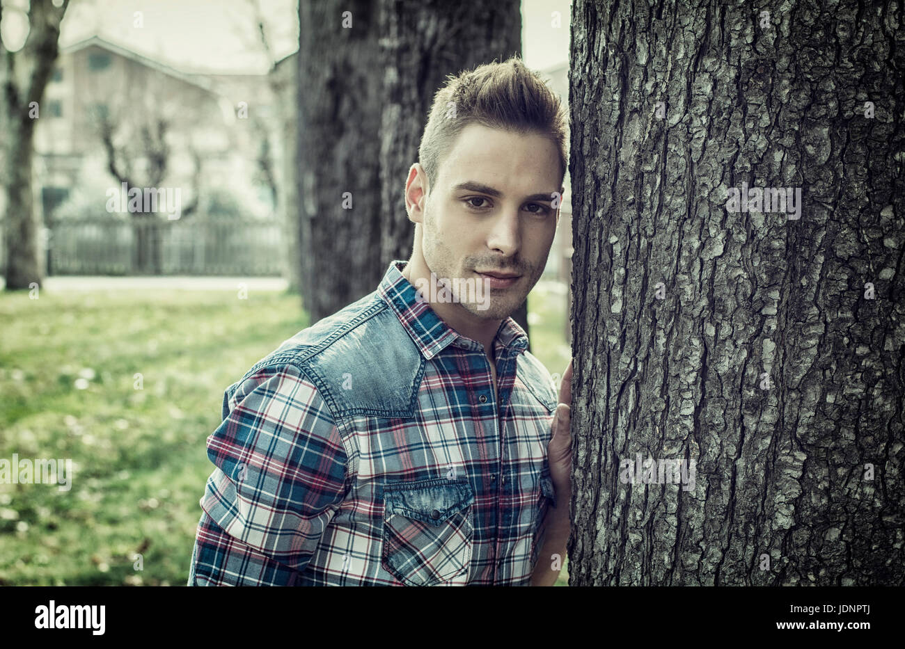 A young man outdoors against a tree, at sunset, with sun behind him ...