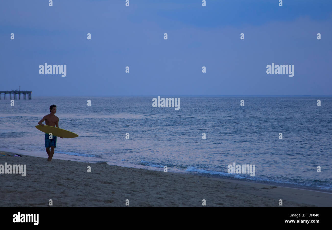 Lone Surfer waiting on beach looking out over water holding surfboard ...