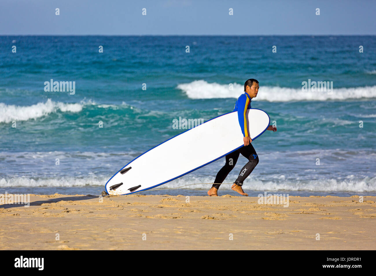 Asian surfer pulling surfboard along beach Stock Photo - Alamy