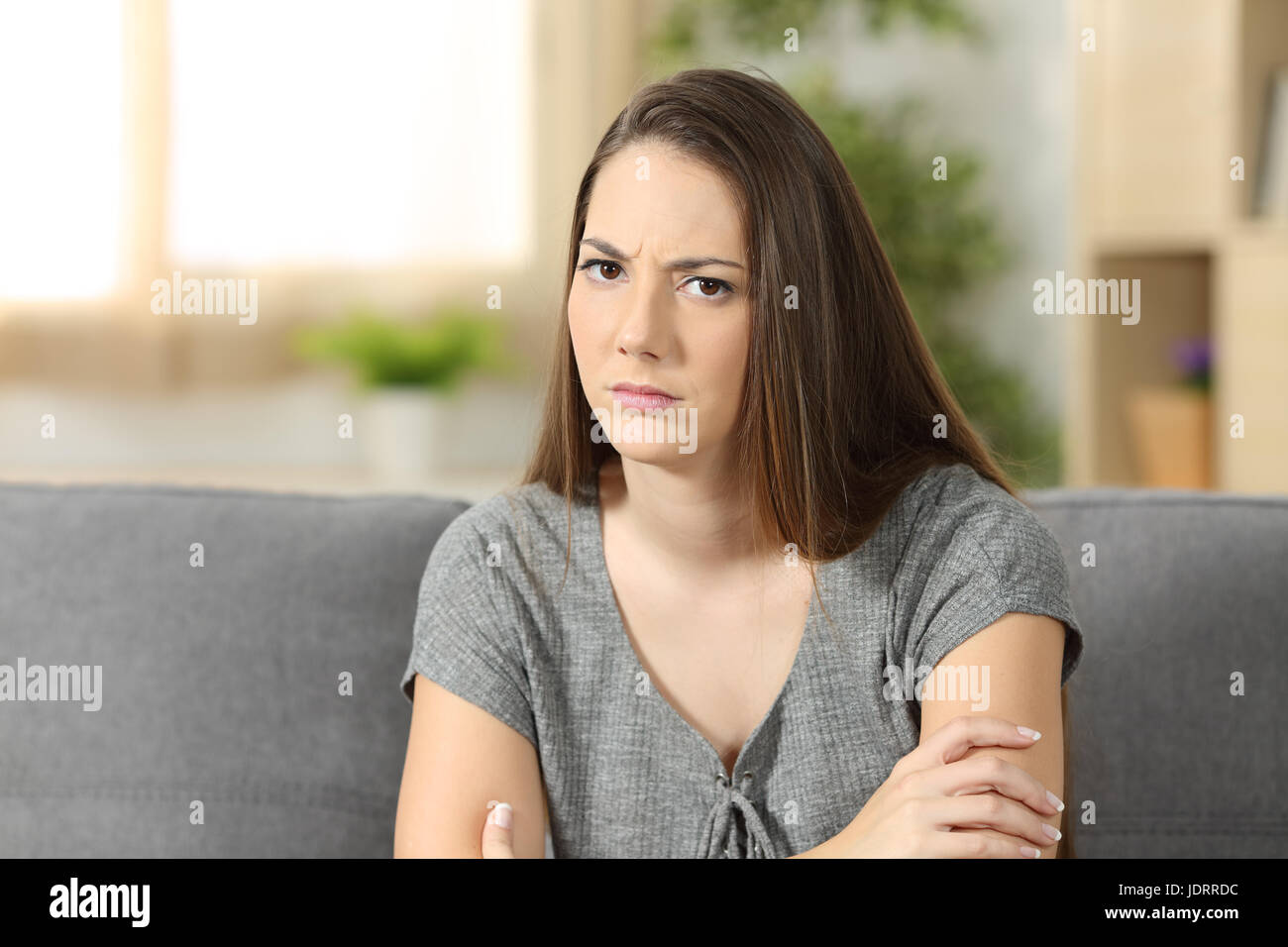 Angry woman looking at you sitting on a sofa in the living room at home ...