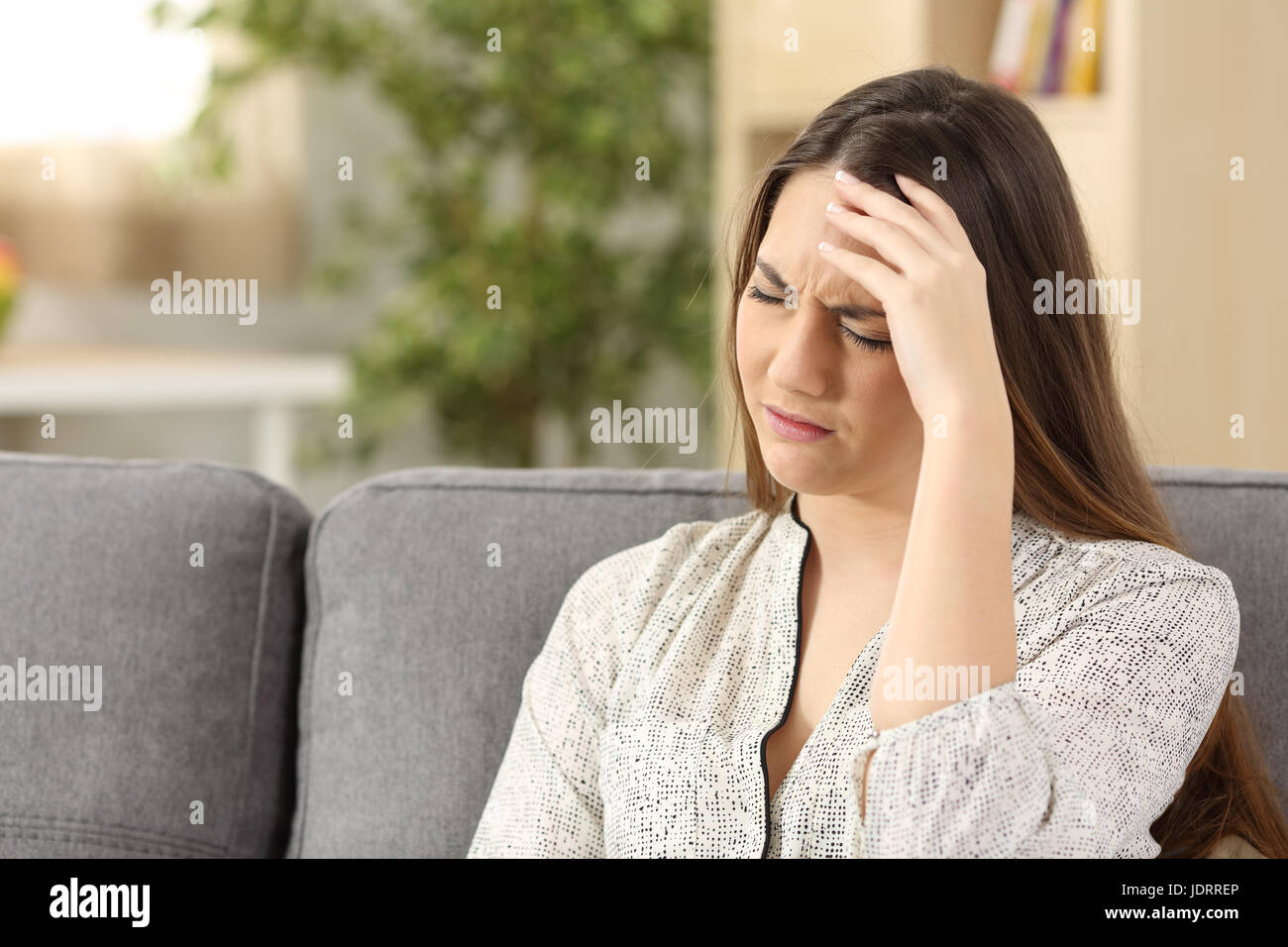 Lady suffering head ache sitting on a sofa in the living room at home ...