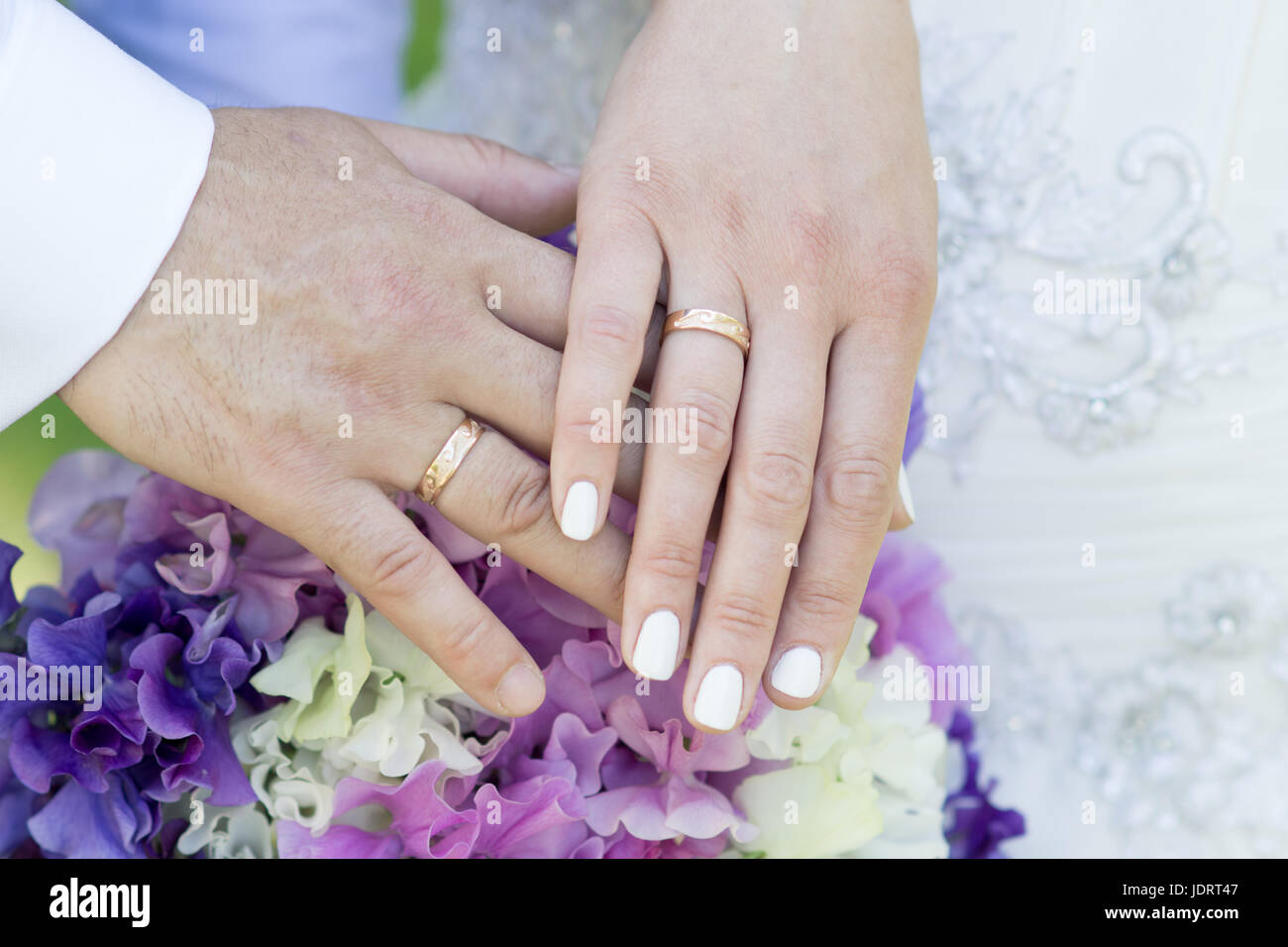 Hands of just married couple with golden wedding rings and sweet pea ...