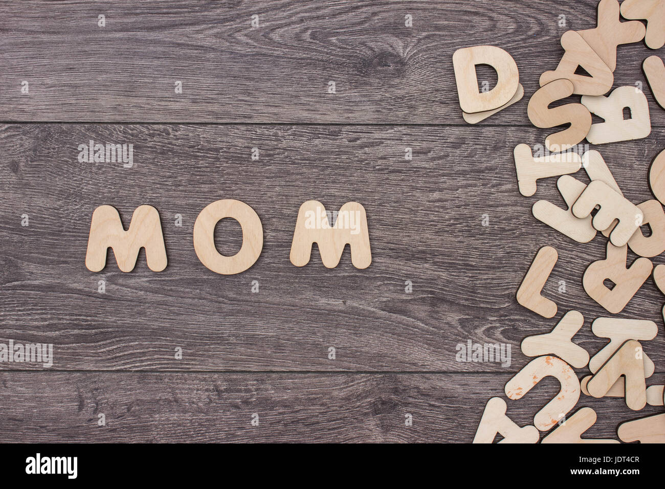 Word Mom made with wooden letters next to a pile of other letters over ...