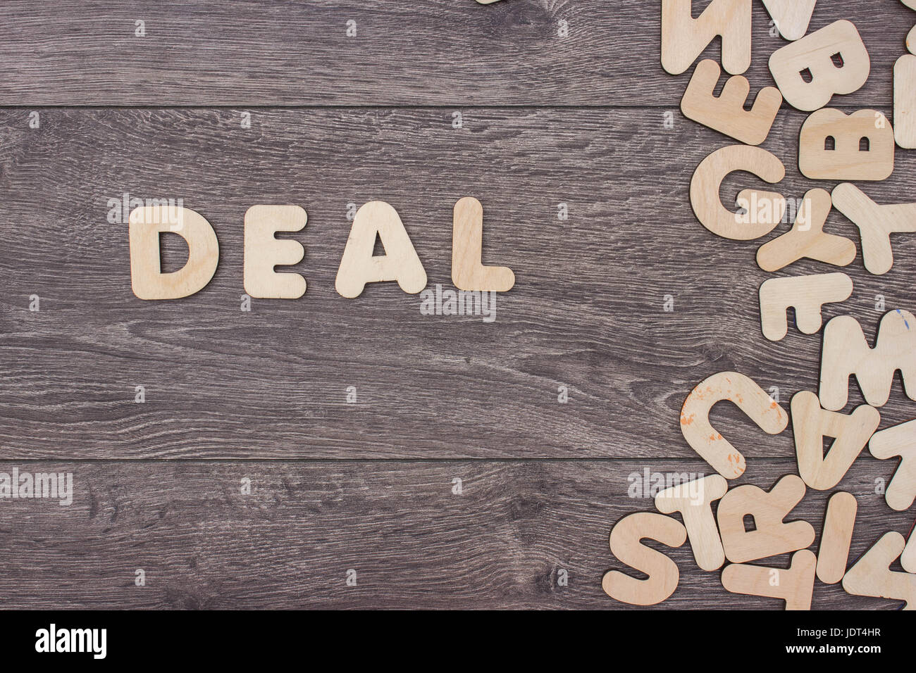 Word Deal made with wooden letters next to a pile of other letters over ...
