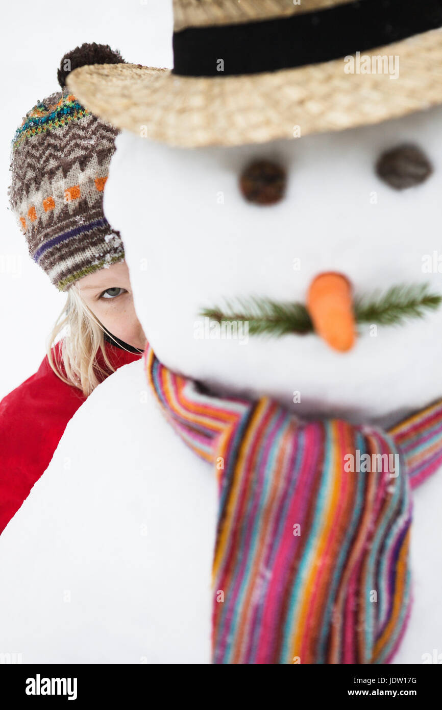 Girl peering out from behind snowman Stock Photo - Alamy