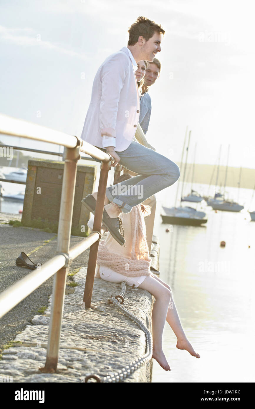 Couples sitting on railing of harbor Stock Photo - Alamy