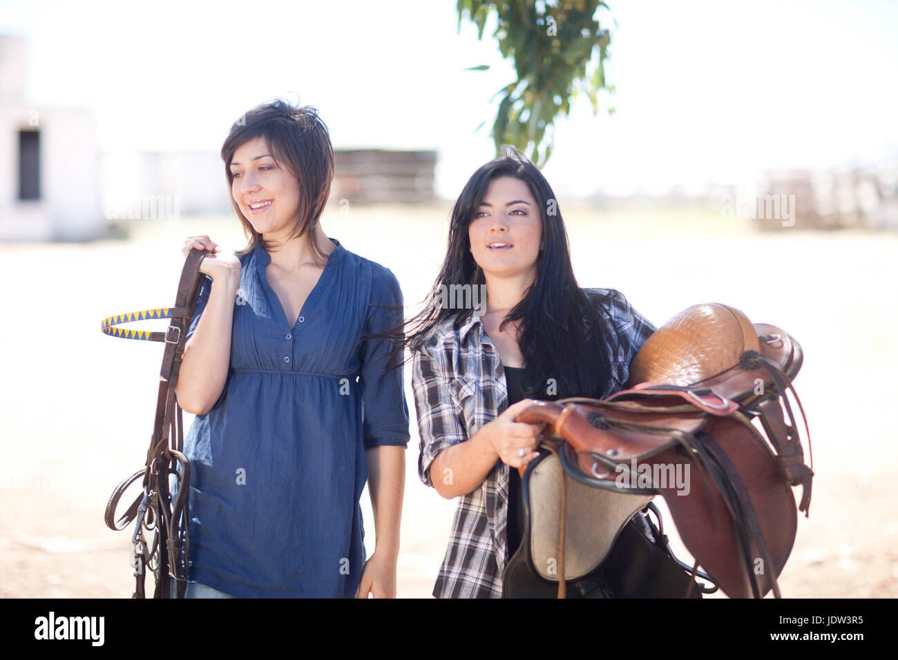 Young women carrying saddle and rope Stock Photo - Alamy