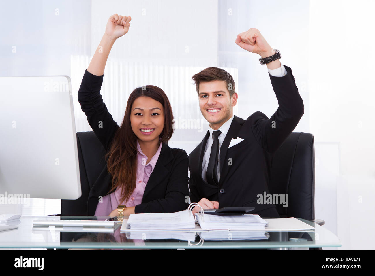 Portrait of successful accountants with hands raised sitting at desk in ...