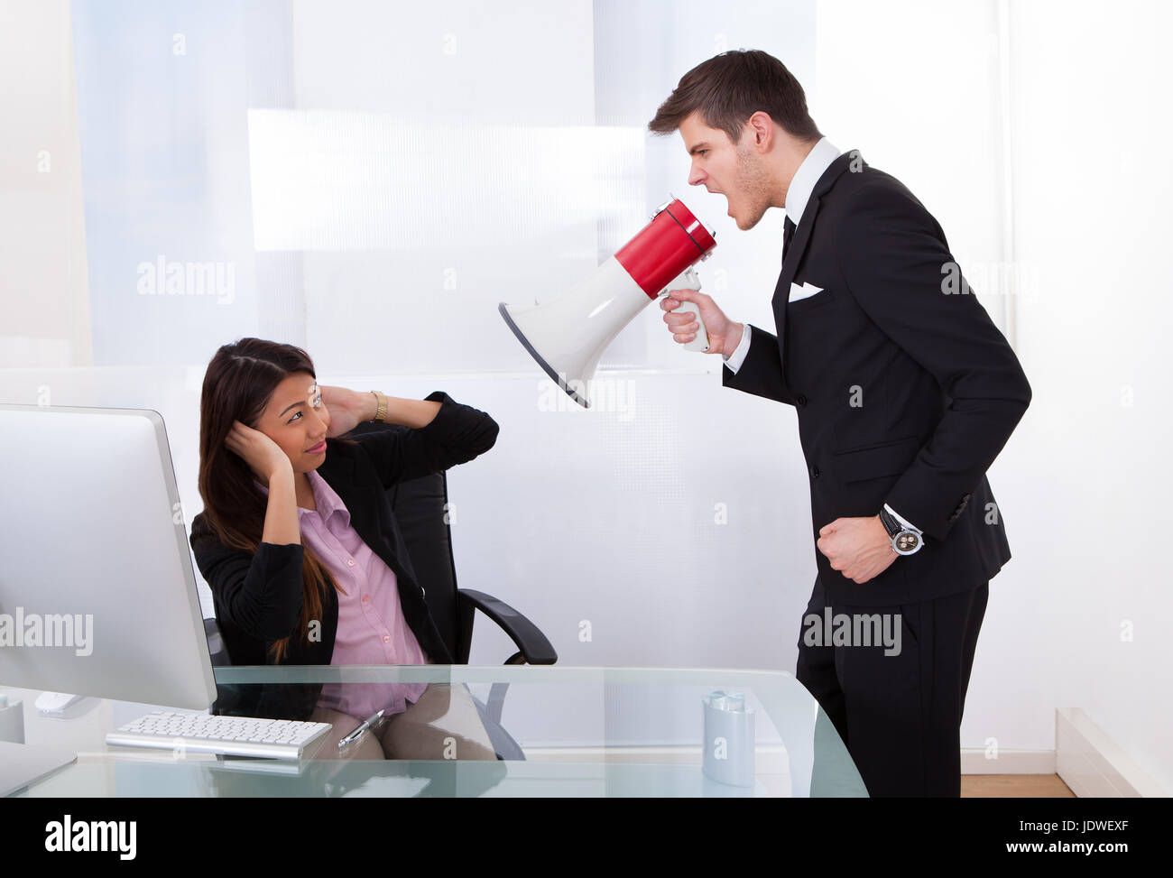 Angry businessman shouting through megaphone on businesswoman in office ...