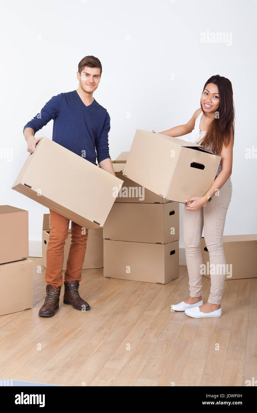 Full length portrait of young couple carrying cardboard boxes at new ...