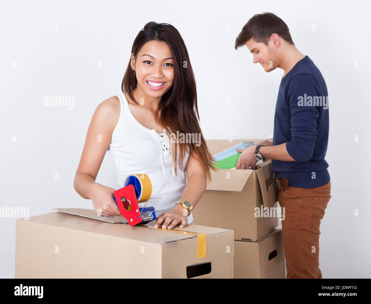 Young woman packing cardboard box with man standing in background at ...