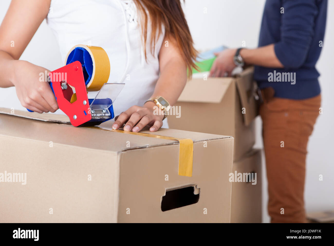 Close-up view of woman packing cardboard box with man standing in ...
