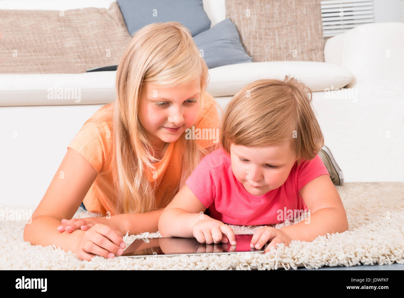 Kids Using Tablet Lying On Carpet At Home Stock Photo - Alamy