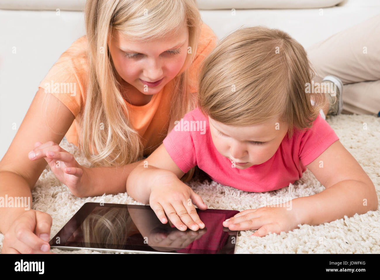 Kids Using Tablet Lying On Carpet At Home Stock Photo - Alamy