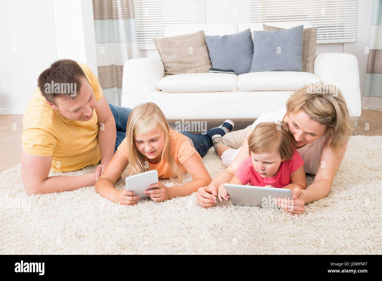 Family Using Tablets Lying On Carpet At Home Stock Photo - Alamy