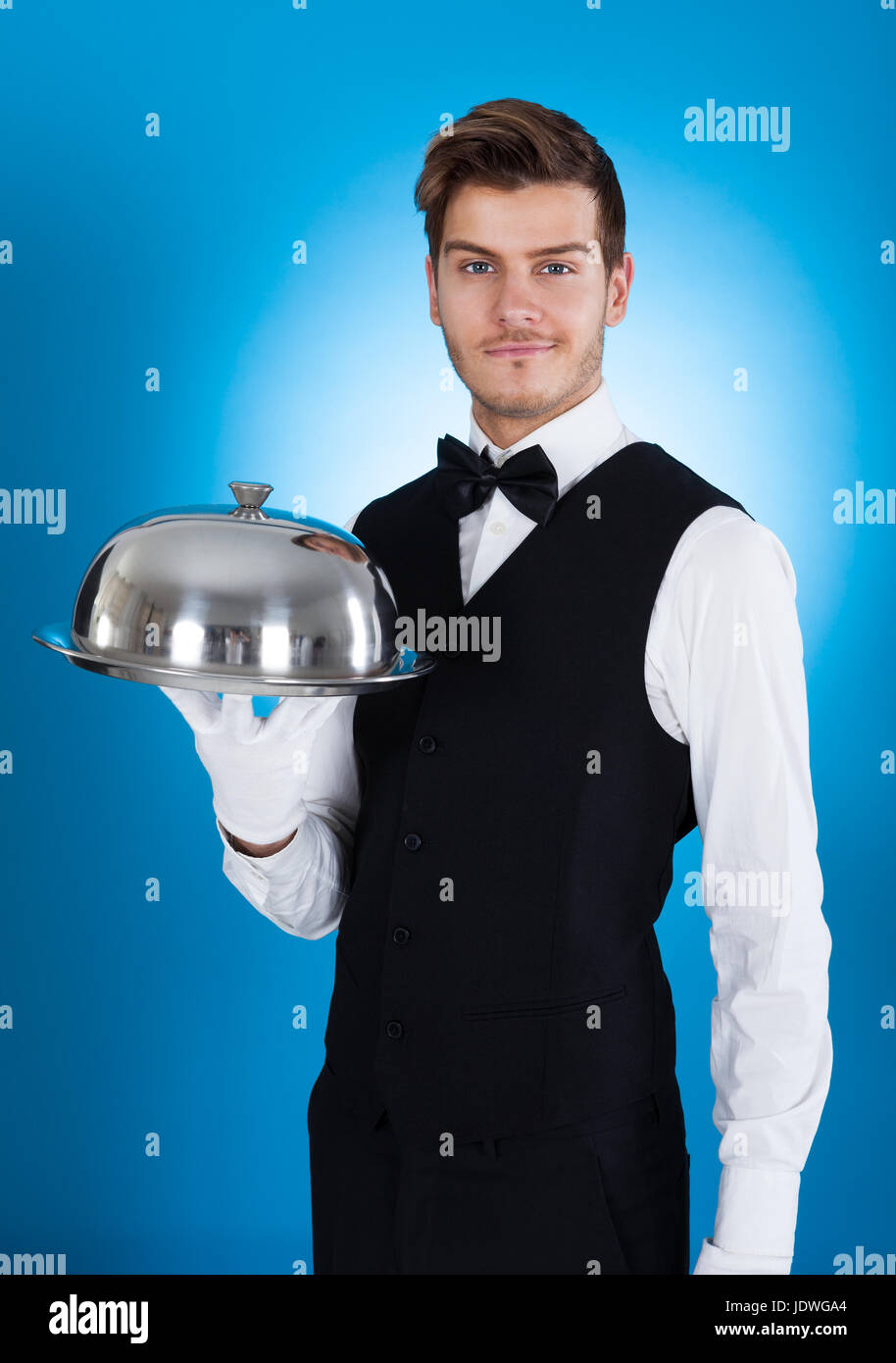 Portrait of confident butler carrying tray over blue background Stock ...
