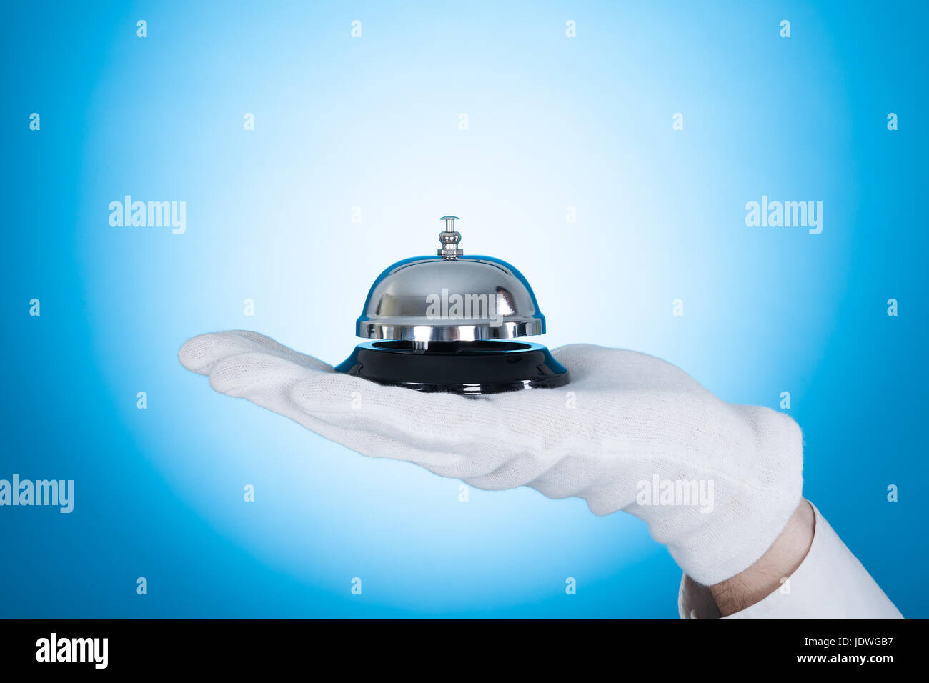 Cropped image of butler holding service bell over blue background Stock ...