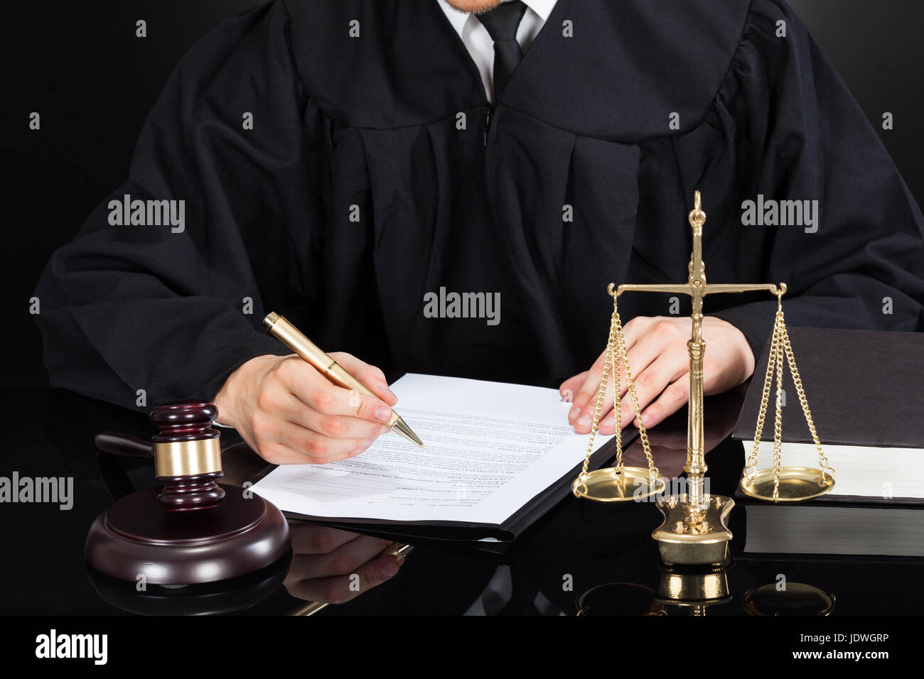 Midsection of male judge writing on paper at desk against black ...